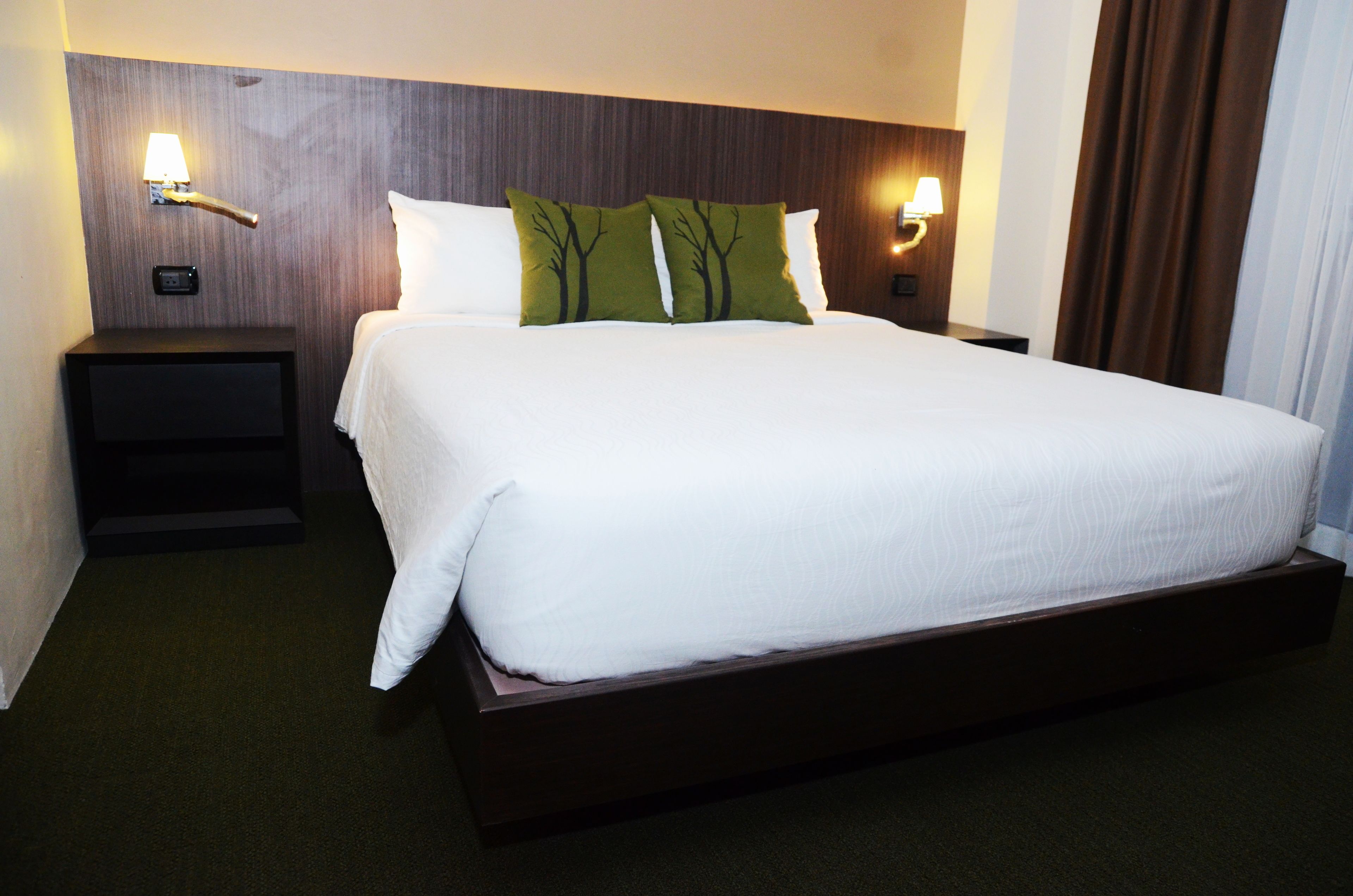 Quarto de hotel com uma cama grande, duas luminárias de cabeceira e uma mesinha de apoio.