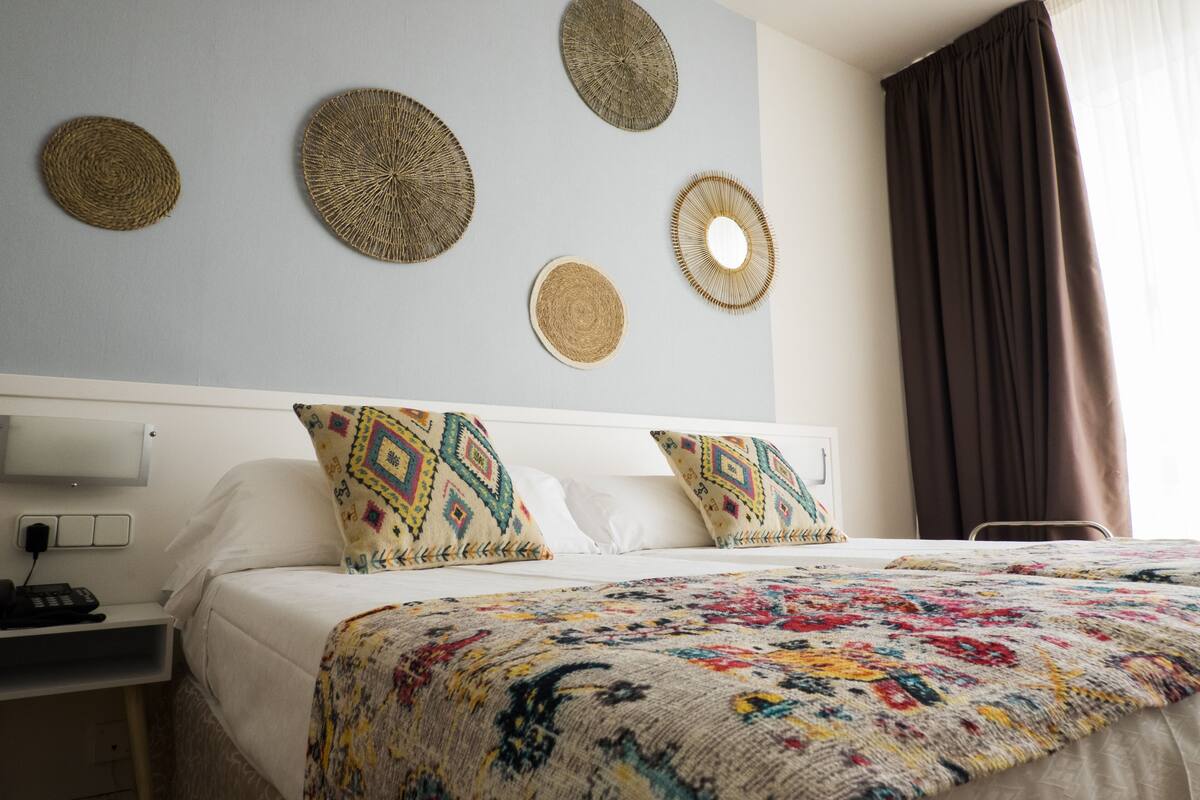 Quarto de hotel com cama, mesa de cabeceira, telefone e arte de parede trançada decorativa.