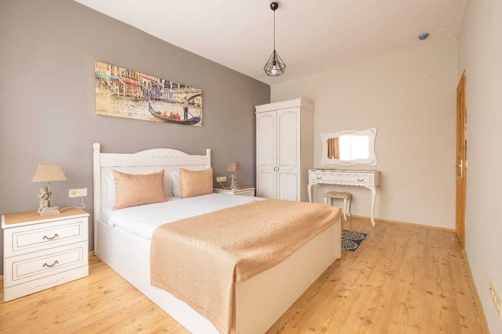 Quarto com cama, mesas de cabeceira, cômoda, penteadeira e um quadro na parede.