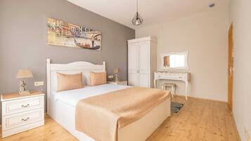 Quarto com cama, mesas de cabeceira, cômoda, penteadeira e um quadro na parede.