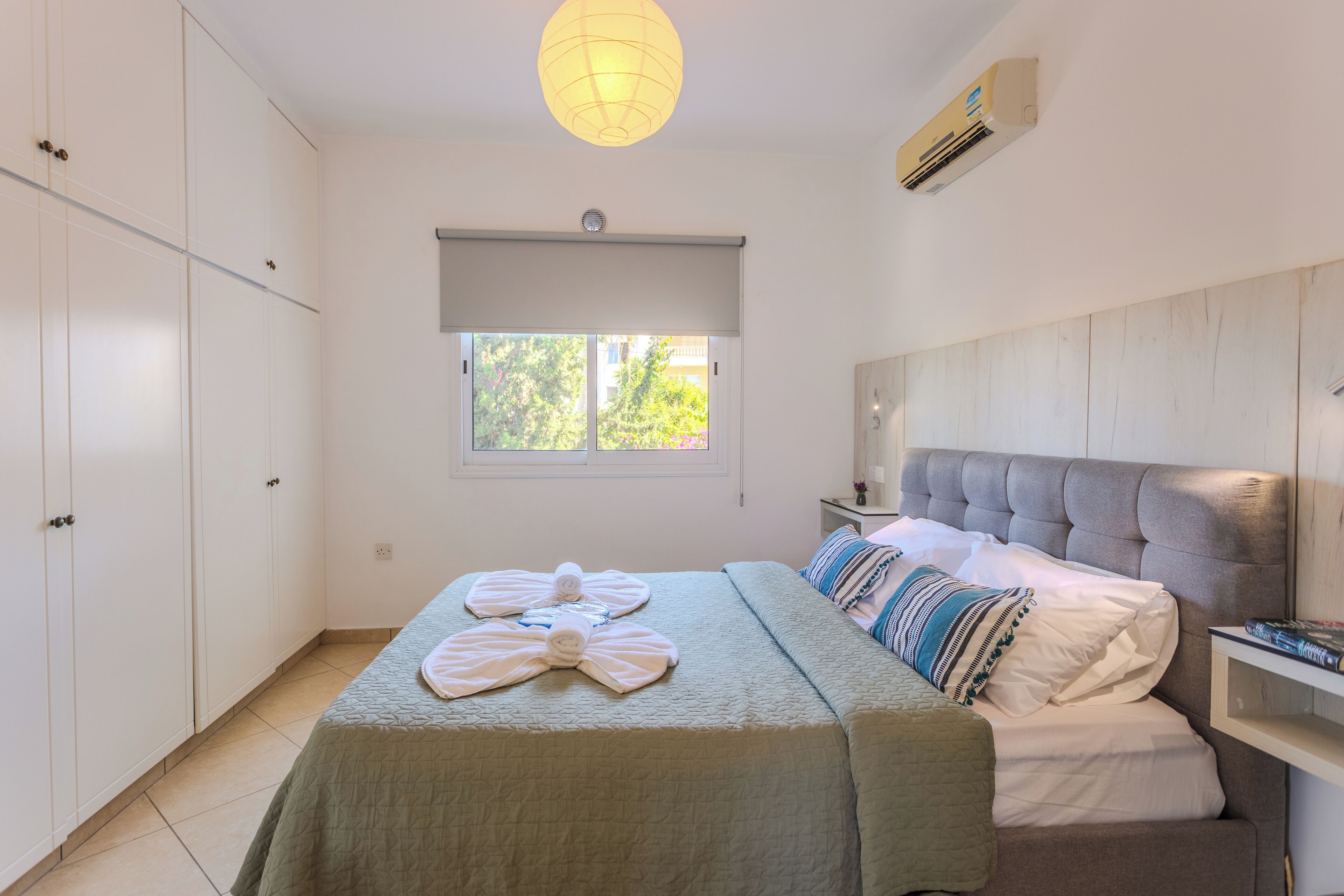 Quarto com cama, janela, luminária no teto e ar-condicionado fixado na parede.