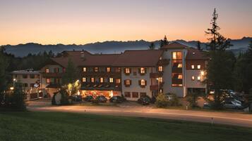 Hotel de vários andares com um pátio central, rodeado por uma área de estacionamento e ao fundo, uma montanha.