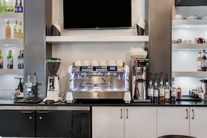 Uma área de bar com uma máquina de café, prateleiras com garrafas e uma televisão acima.