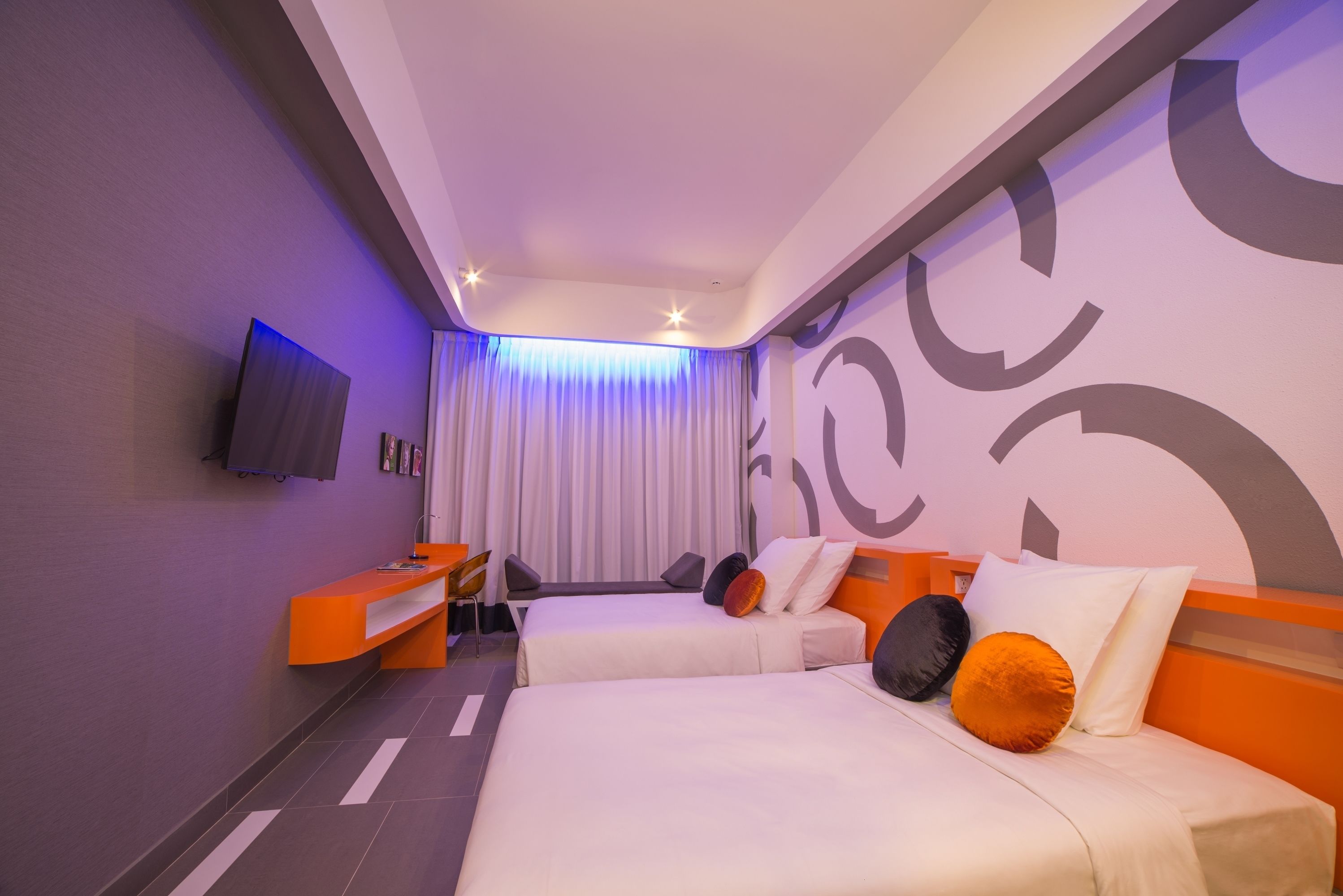 Quarto de hotel moderno com duas camas, televisão de tela plana, escrivaninha e uma janela grande com cortinas.