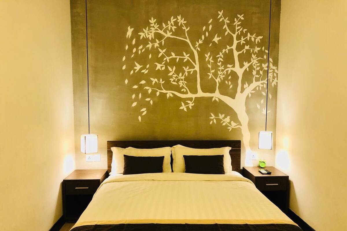 Quarto de hotel com uma cama grande, duas mesas de cabeceira e um mural na parede com uma árvore.