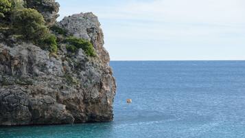 Costa rochosa com mar azul límpido e uma bóia na água.