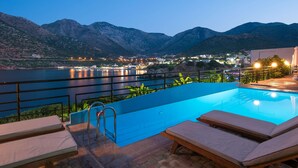 Piscina infinita com vista para um lago e montanhas, cadeiras de descanso e um corrimão.
