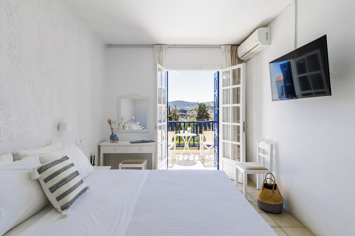 Quarto de hotel com cama, escrivaninha, cadeira, televisão e varanda com vista para a cidade.