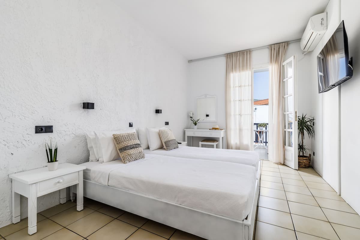Quarto com duas camas, mesa de cabeceira, cômoda, televisão e janela com cortinas.