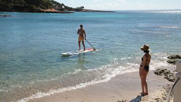 Uma cena de praia com uma pessoa praticando paddleboard e outra pessoa na costa.