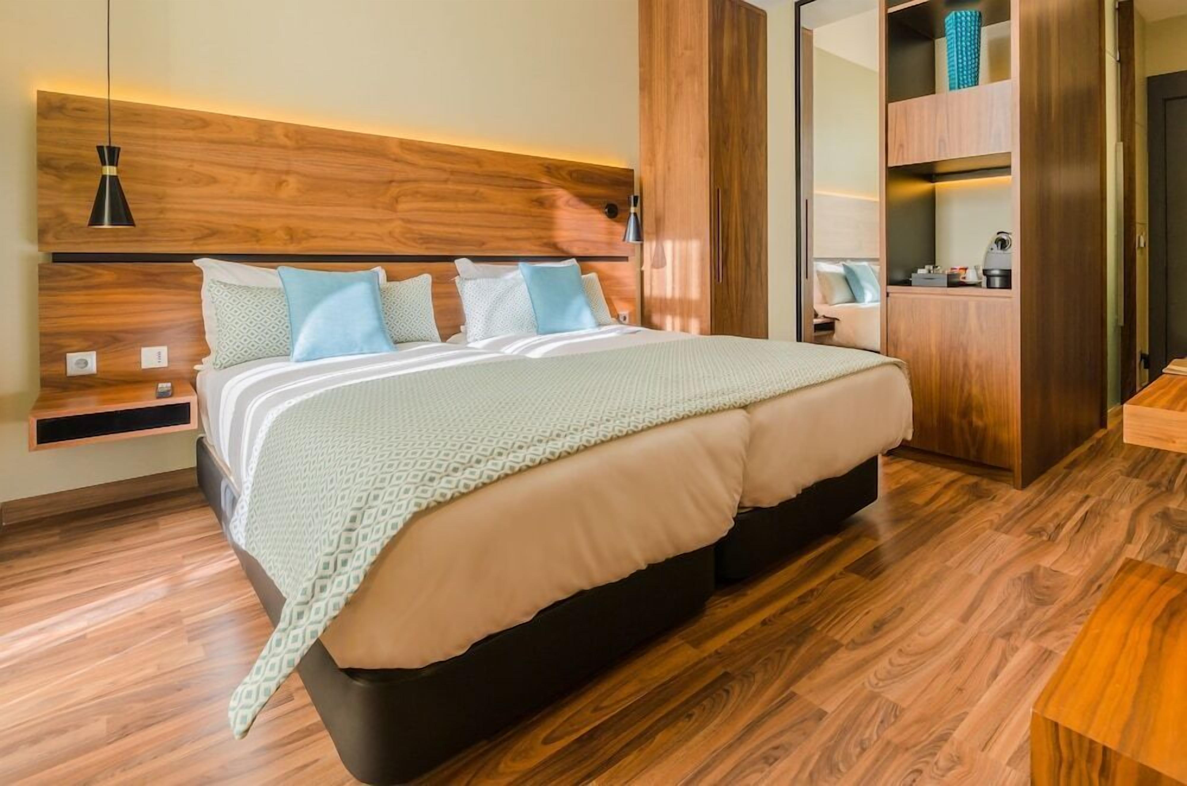 Quarto moderno com cabeceira de madeira, cama com roupa de cama estampada, mesa de cabeceira e guarda-roupa.
