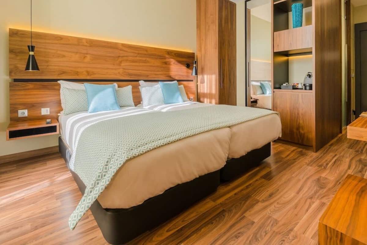 Quarto moderno com cabeceira de madeira, cama com roupa de cama estampada, mesa de cabeceira e guarda-roupa.