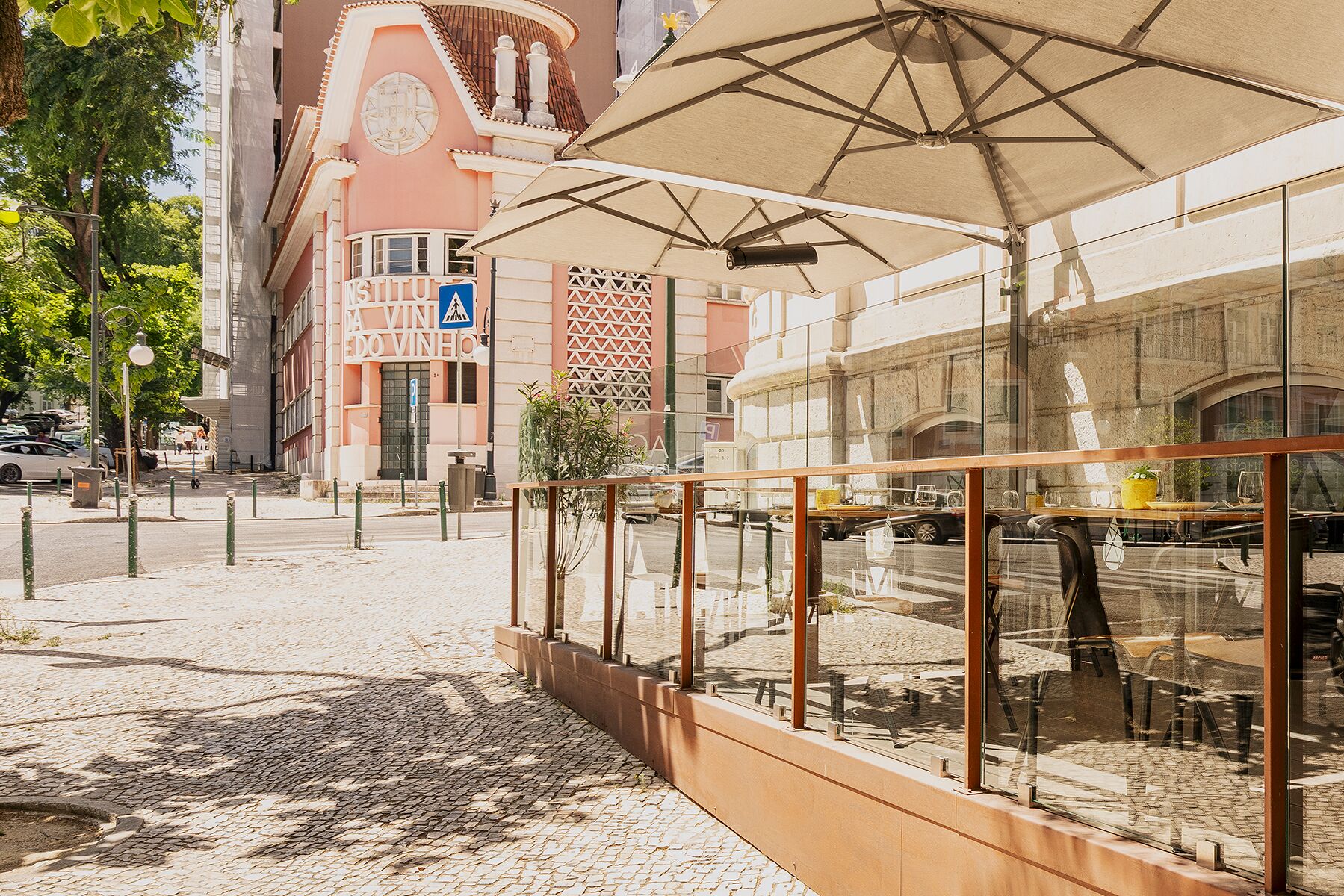 Uma área de estar ao ar livre com estrutura de vidro, vista para a rua e um edifício com uma placa que diz 'A Vinho do Vinho'.