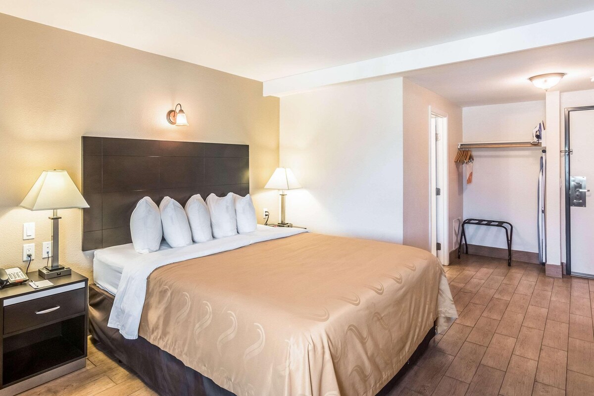 Quarto de hotel com uma cama grande, duas mesas de cabeceira com luminárias, uma cabeceira e um guarda-roupa.