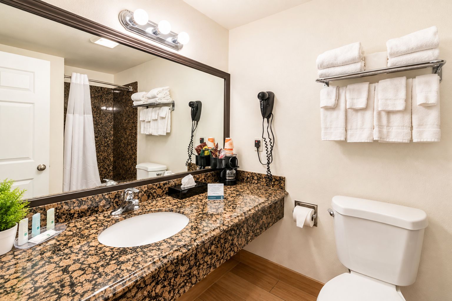 Casa de banho com lavatório de bancada em granito, sanita, suporte para toalhas e secador de cabelo.