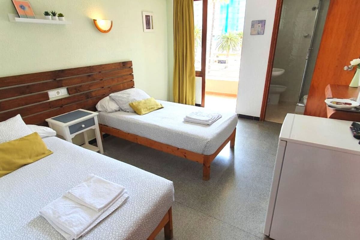 Quarto de hotel com duas camas, uma secretária pequena, casa de banho e zona de duche.