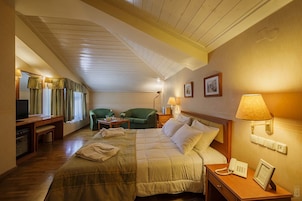 Quarto de hotel com uma cama grande, uma escrivaninha com televisão, uma poltrona verde e um abajur.