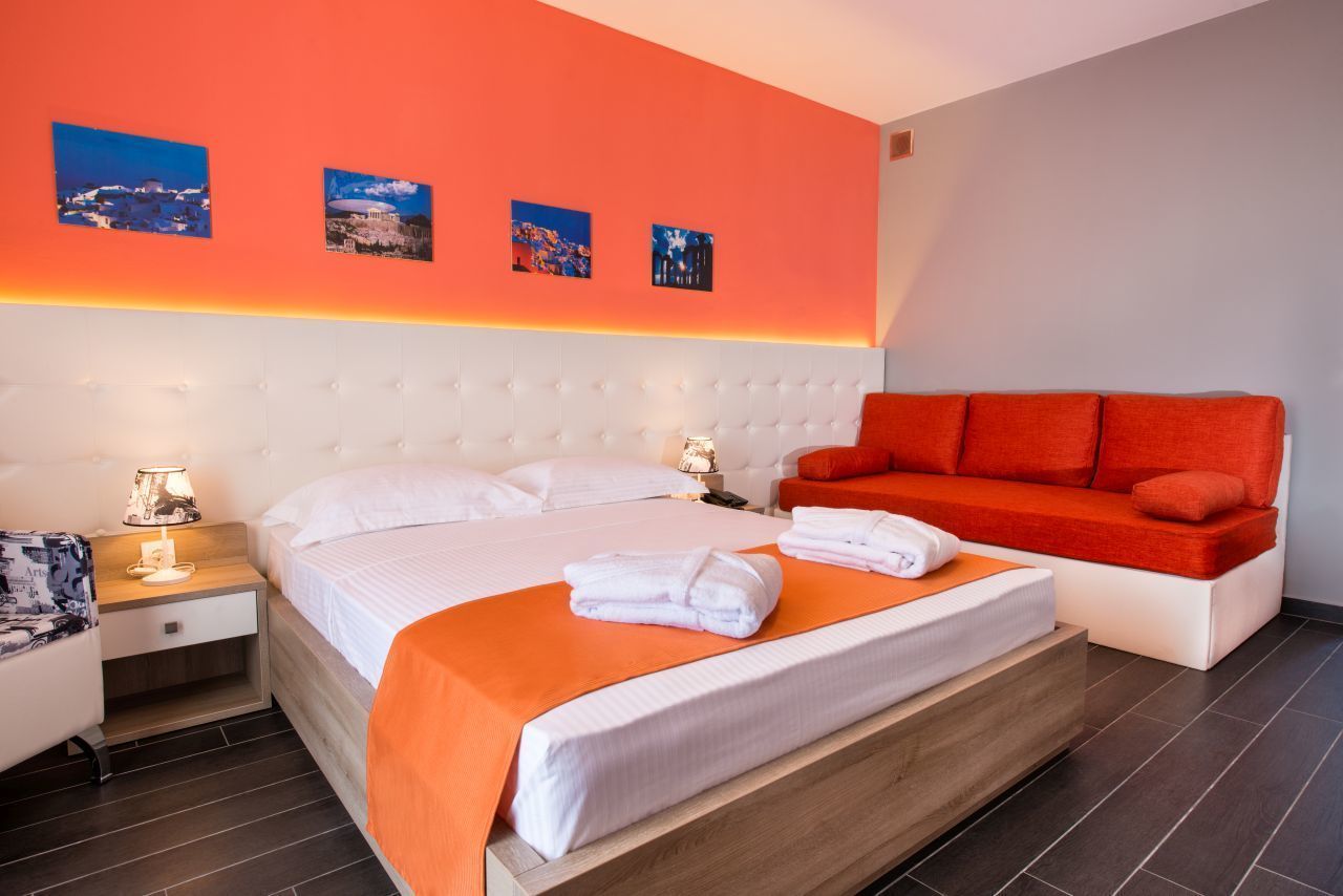 Quarto de hotel com uma cama grande, um sofá vermelho e uma mesa de cabeceira com abajur.