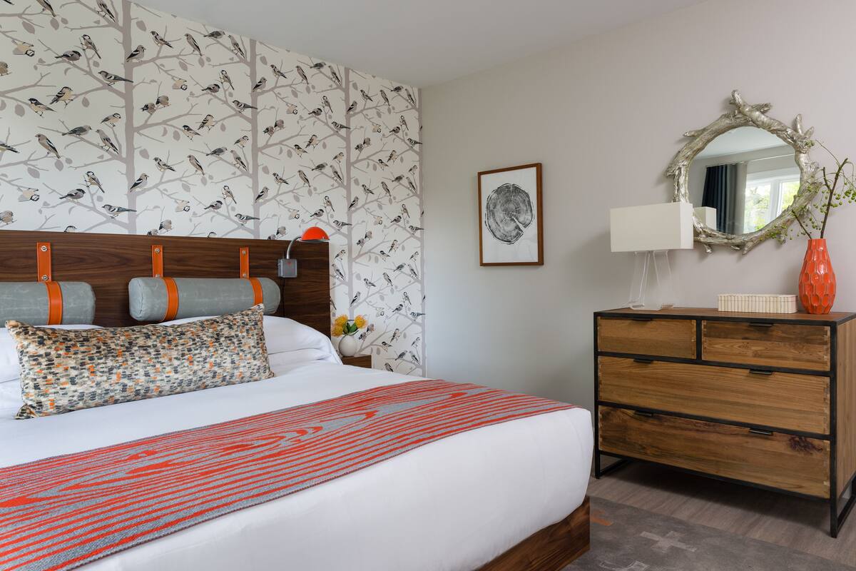Quarto com cama, penteadeira, espelho e parede com padrão de pássaros.