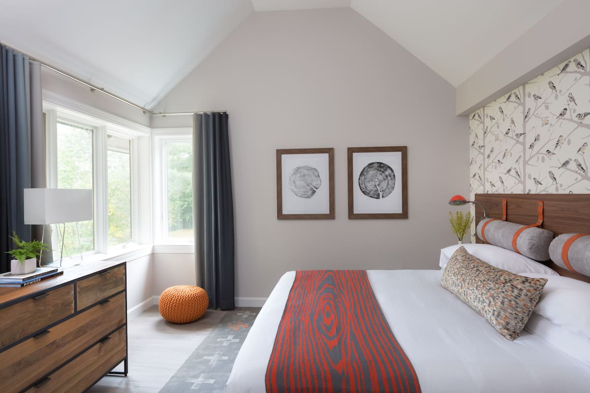 Quarto moderno com cama grande, cômoda de madeira e janela com cortinas.