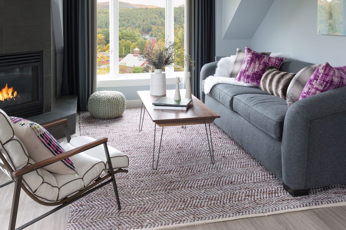 Uma sala de estar moderna com lareira, sofá cinza e vista para o exterior.