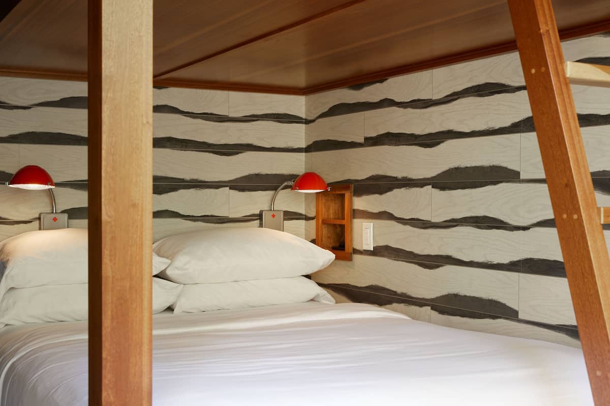 Uma cama beliche com roupa de cama branca e abajures vermelhos de cada lado.