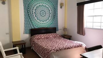 Quarto com cama, cadeira, mesa pequena, tapeçaria e janela com cortinas.