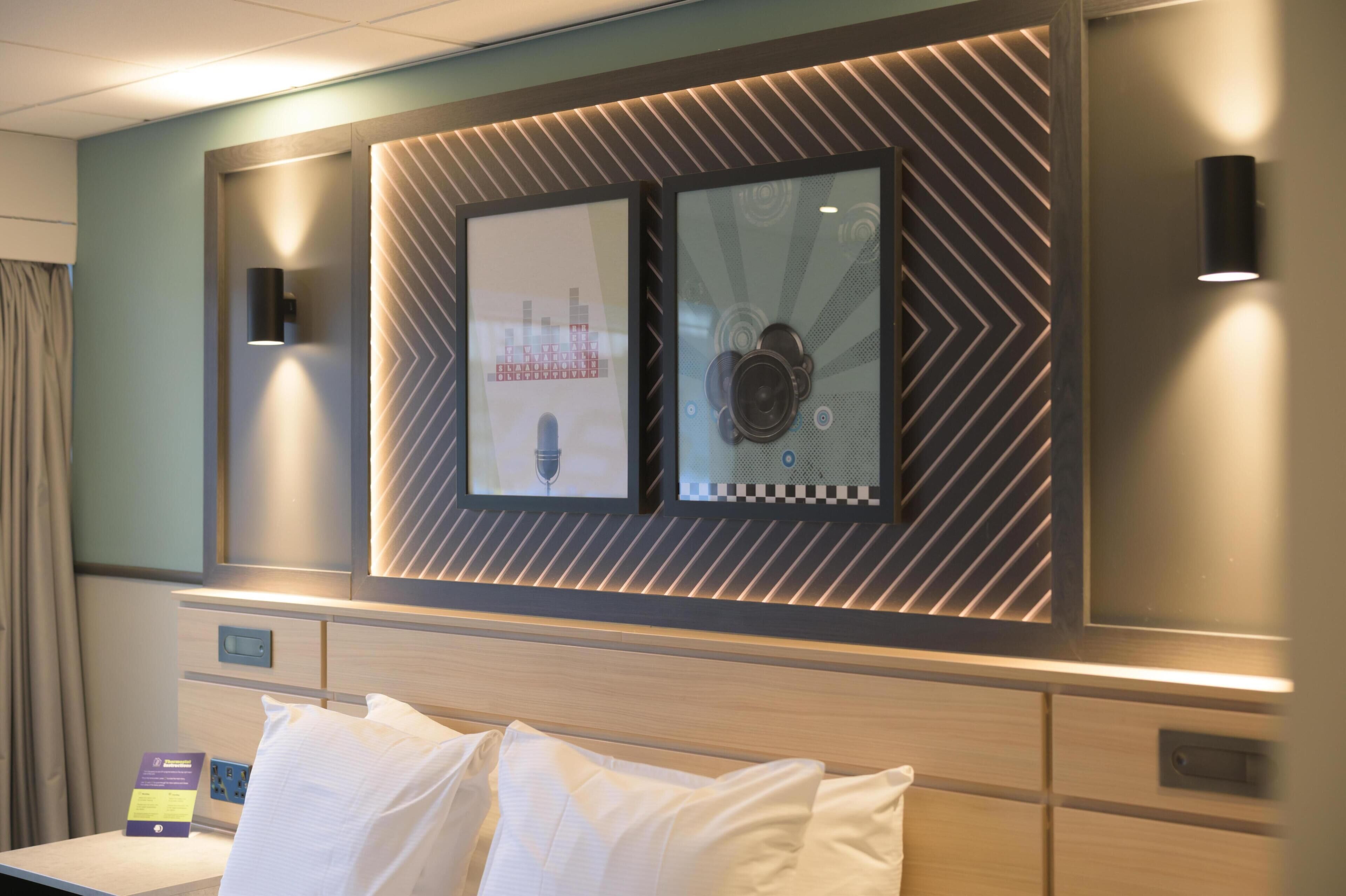 Quarto de hotel com cama, televisão na parede e painel de comando.