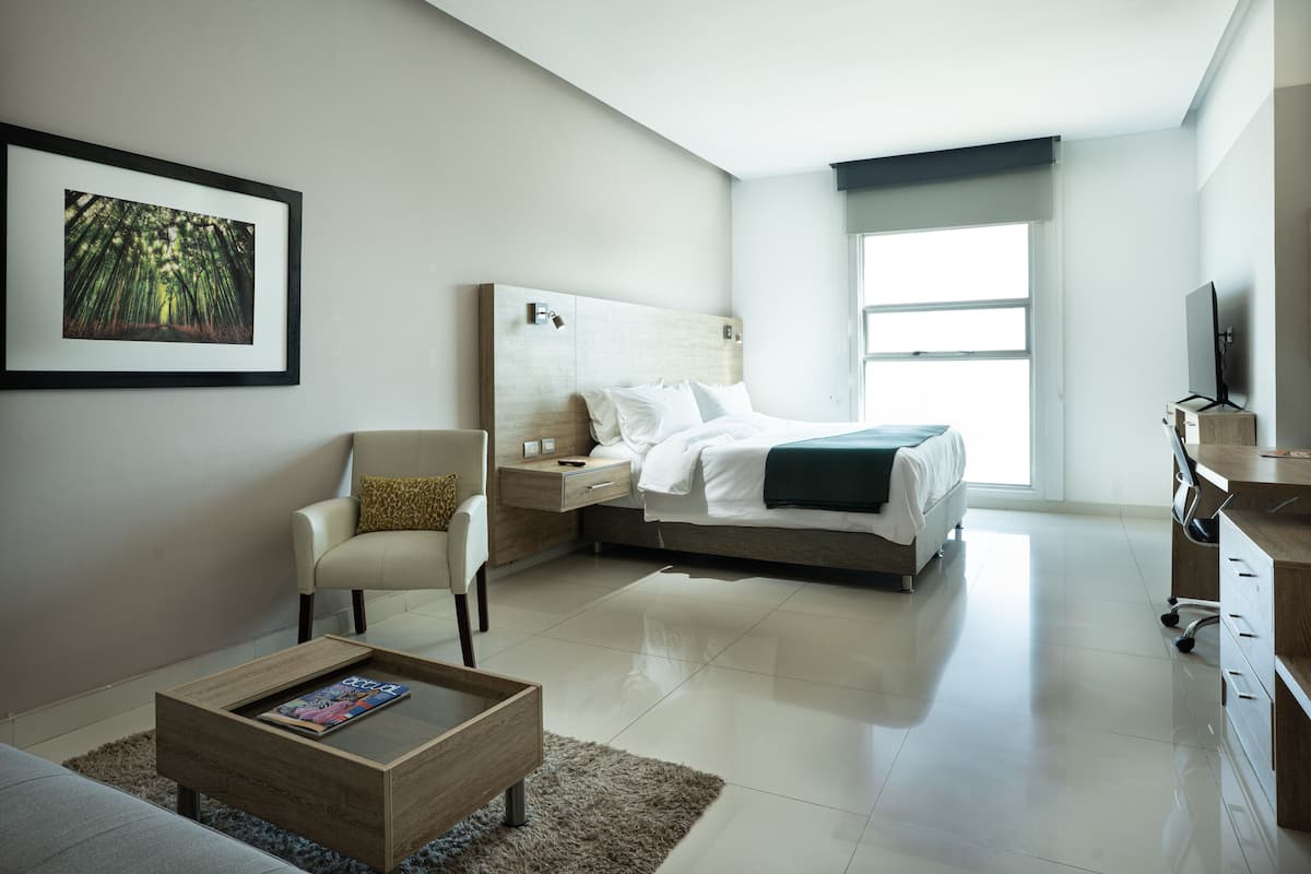 Um quarto moderno com uma cama, mesas de cabeceira, uma cadeira, uma escrivaninha e uma janela grande.