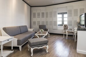 Uma sala de estar moderna com um sofá cinzento, poltronas brancas, uma pequena mesa com um vaso e uma televisão.