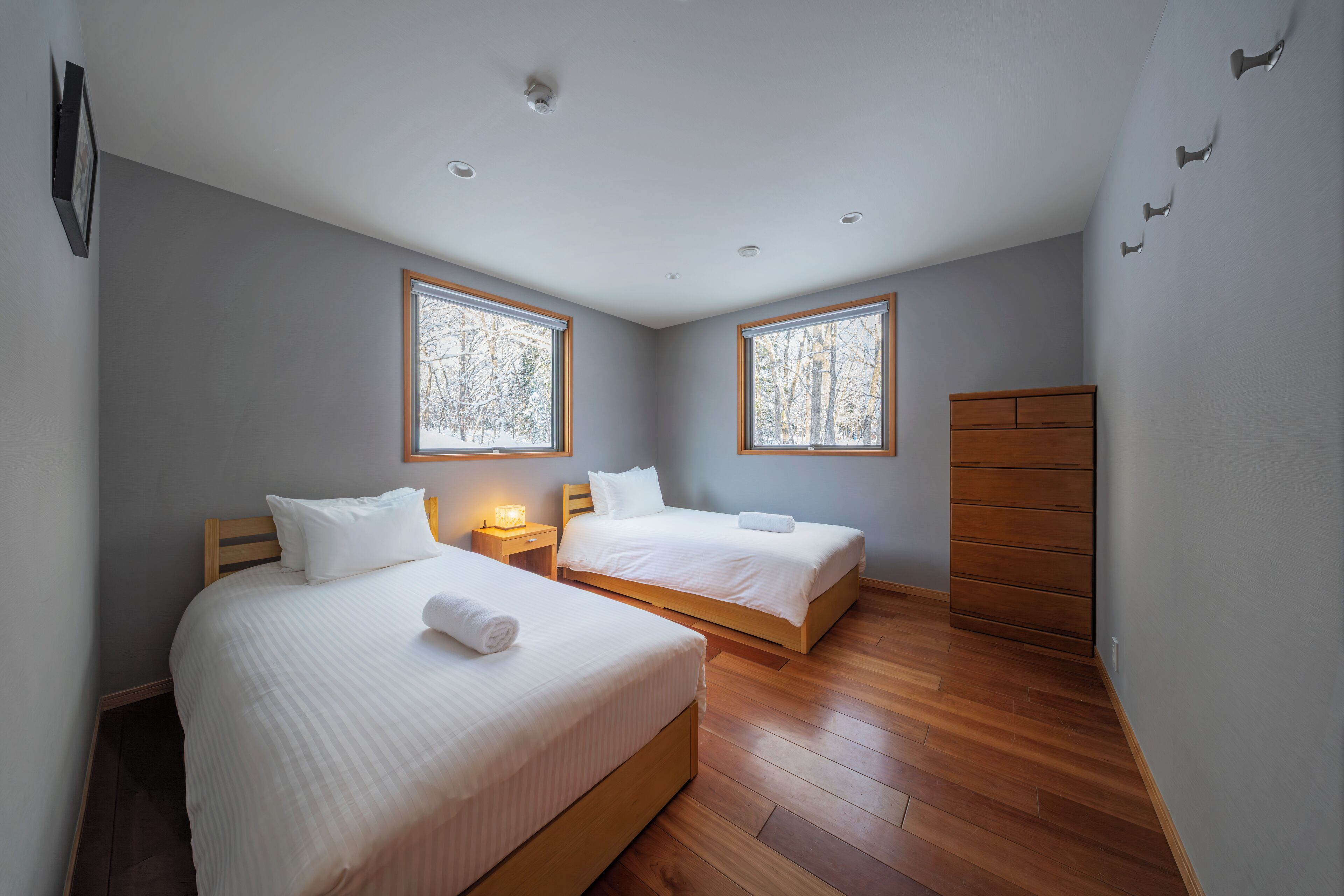 Quarto com duas camas, piso de madeira e grandes janelas.