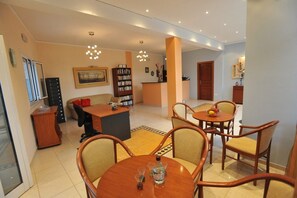Uma área de refeições com mesa e cadeiras de madeira, uma estante e um pequeno espaço de cozinha.