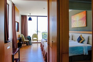 Quarto de hotel com cama, escrivaninha, cadeira e vista para o exterior.