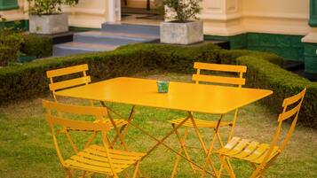Conjunto de mesa e cadeiras amarelas num espaço de jardim, com um edifício ao fundo.