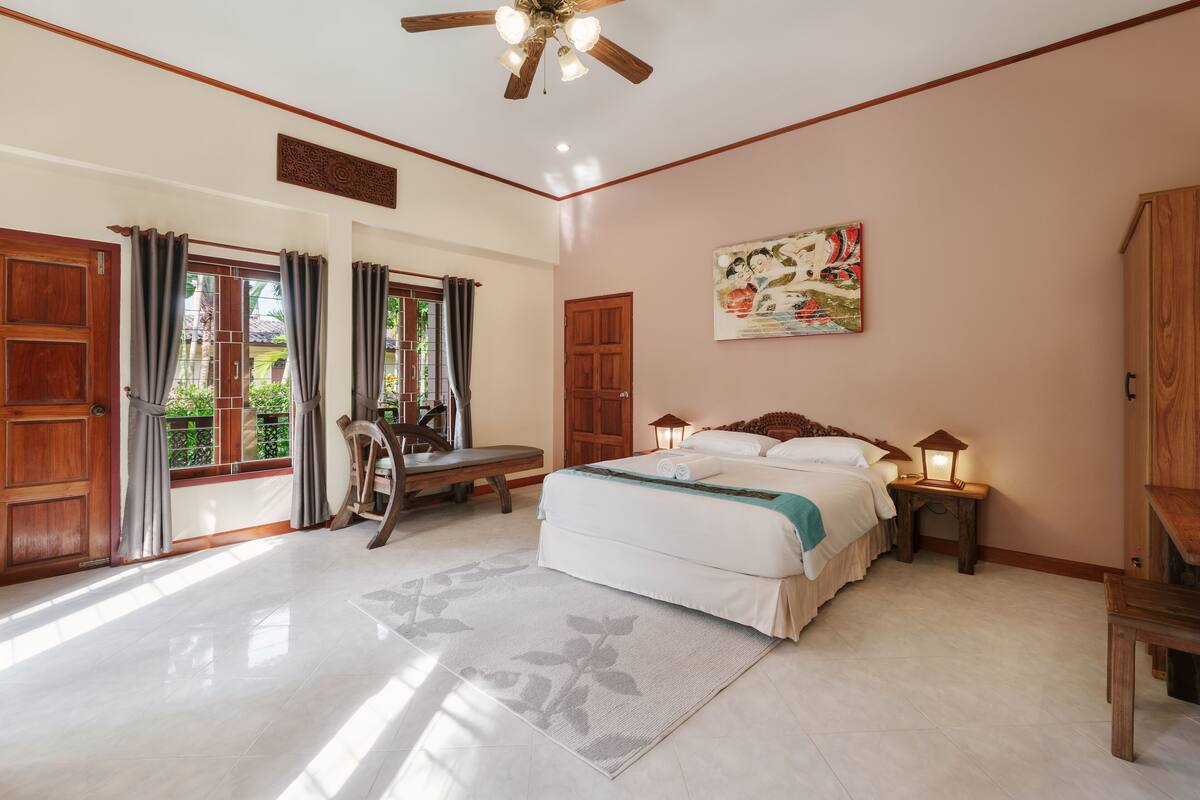 Quarto espaçoso com uma cama grande, mobiliário de madeira e vista para o verde pelas janelas.