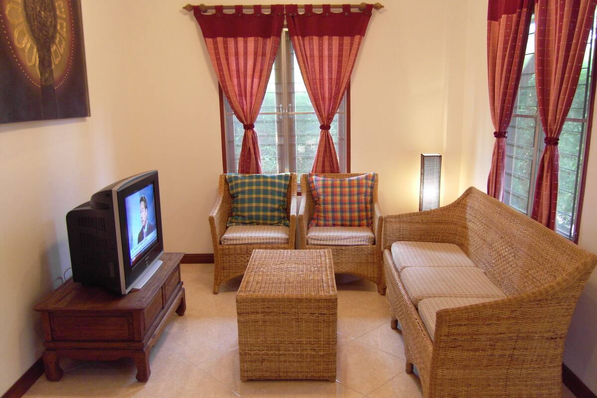 Uma sala de estar com móveis de vime, uma televisão e cortinas vermelhas.