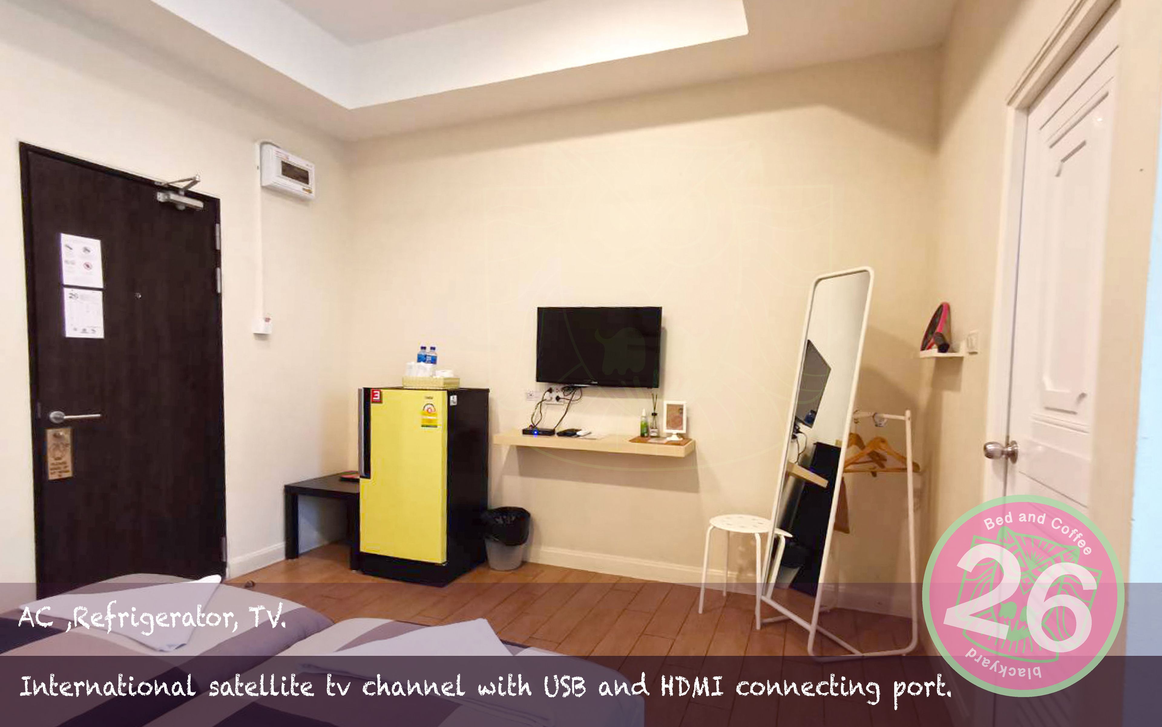 Quarto compacto com cama, escrivaninha pequena, televisão, frigorífico e espelho.