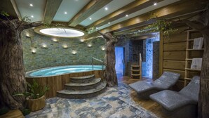 Uma área de spa com hidromassagem, decoração de árvore em madeira, paredes de pedra e espreguiçadeiras.