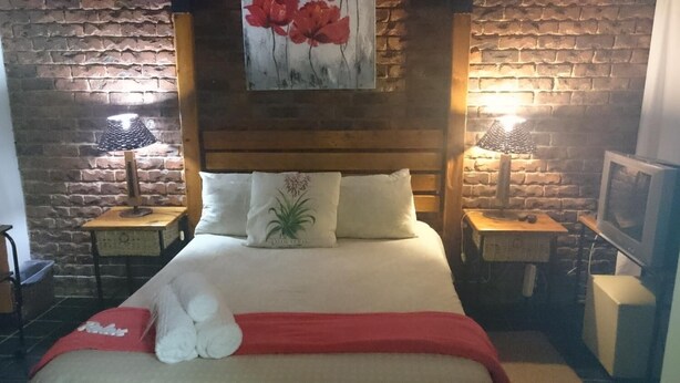 Uma cama com um cobertor vermelho, duas luminárias de cabeceira e um quadro de flores vermelhas na parede de tijolos.