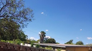 Piscina com duas espreguiçadeiras brancas, um muro de tijolos e um céu azul límpido.