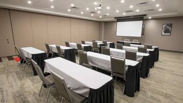 Uma sala de conferência com várias mesas, cadeiras, uma tela de projetor e piso coberto de carpete.