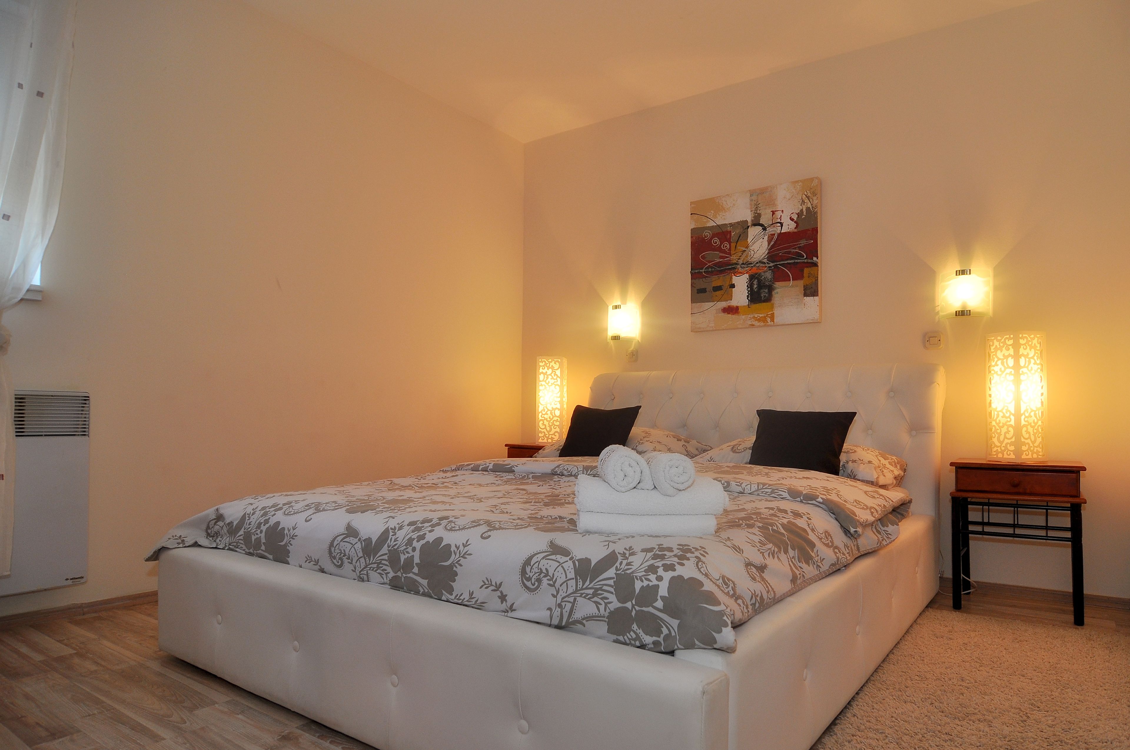 Uma cama bem arrumada com um cobre-leito floral, duas luminárias na parede e um quadro sobre a cama.