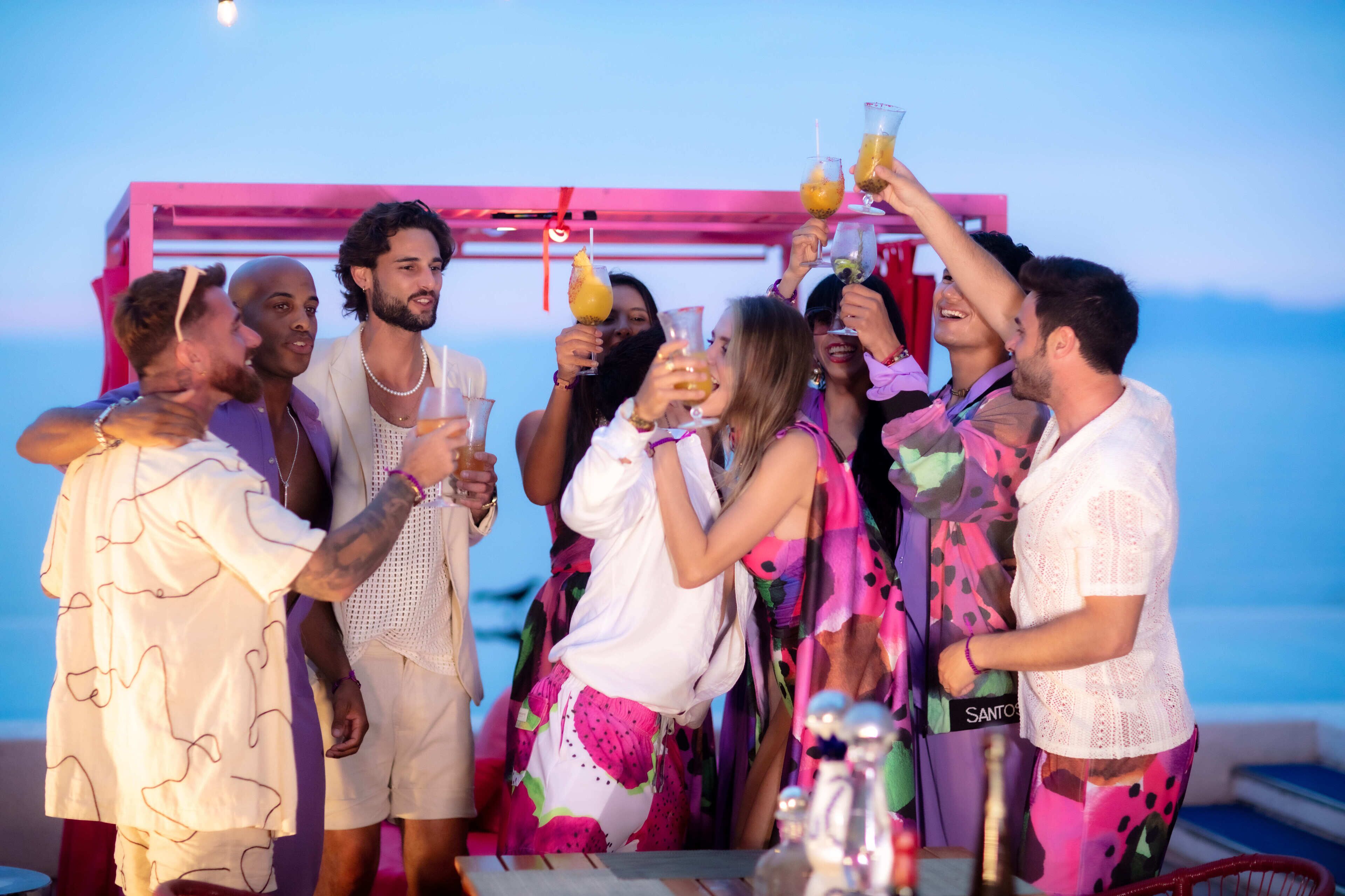 Um grupo de pessoas brindando com bebidas em uma festa em um barco com toldo rosa.