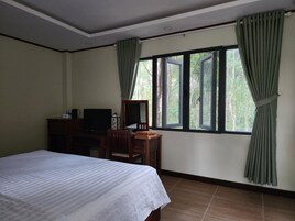 Quarto de hotel com cama, escrivaninha, cadeira, televisão e janela com cortinas.