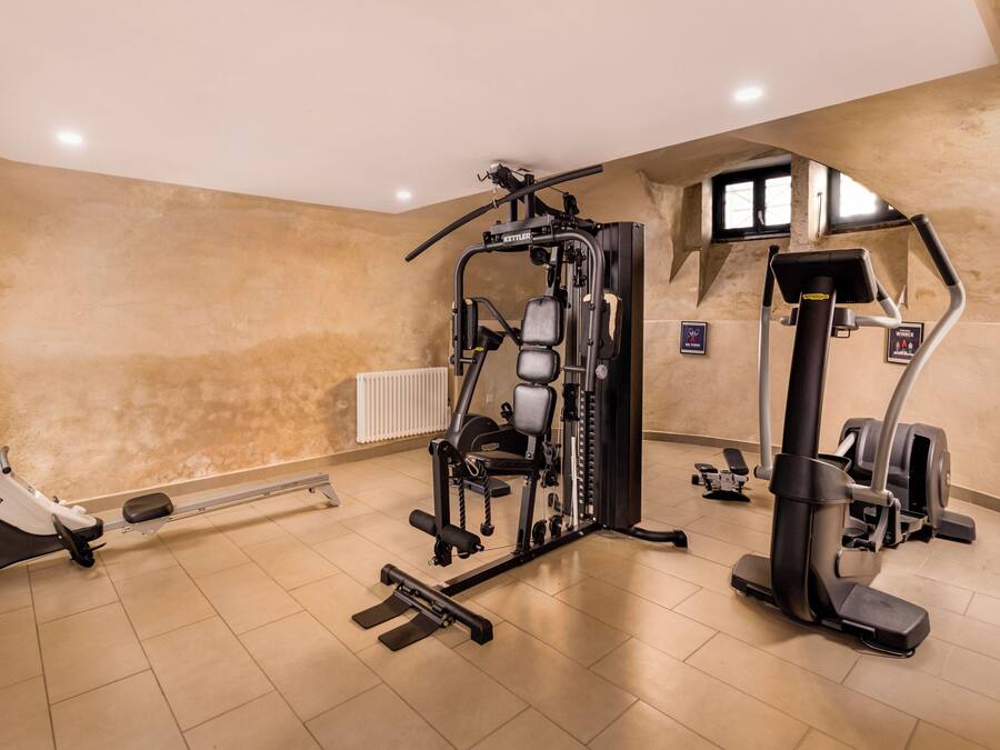 Uma academia com diversos equipamentos de exercício, incluindo uma máquina Kettler, um aparelho de escada e uma esteira.