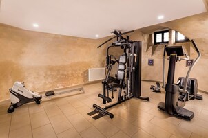Uma academia com diversos equipamentos de exercício, incluindo uma máquina Kettler, um aparelho de escada e uma esteira.