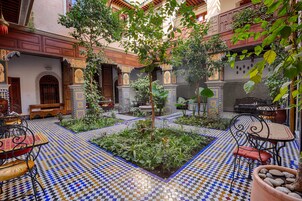 Um pátio com piso de azulejos, uma árvore central e área de estar externa.
