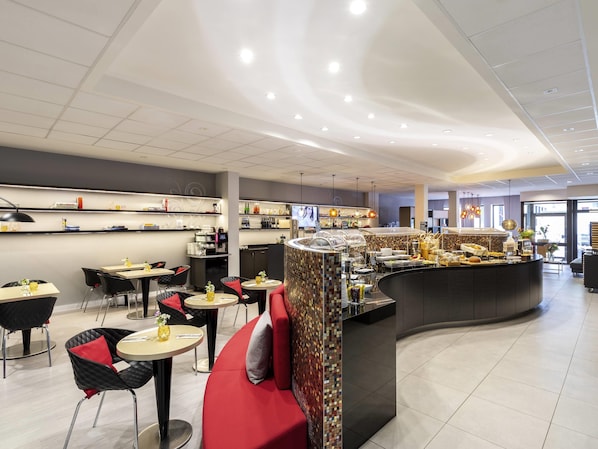 Restaurante moderno com balcão curvo, mesas redondas e assentos acolchoados em vermelho.