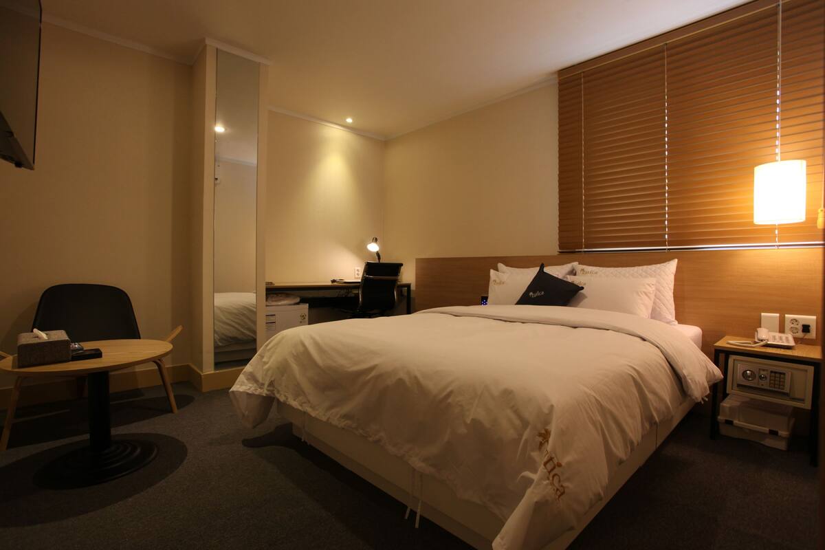 Quarto de hotel com cama grande, mesa de cabeceira, abajur e escrivaninha com cadeira.