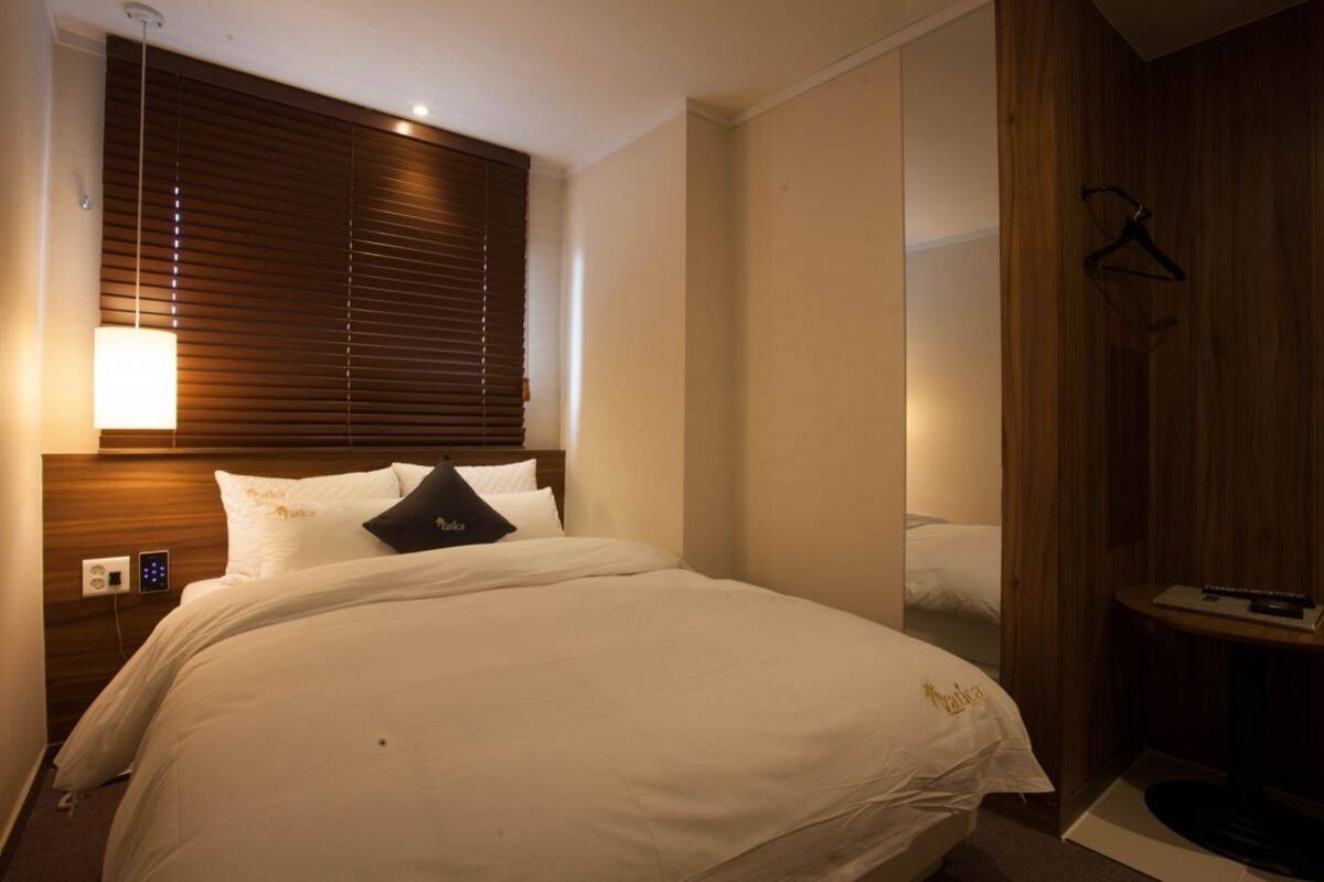 Quarto de hotel com cama grande, cabeceira de madeira, mesa de cabeceira com abajur e um espelho.